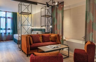 Quarto de hotel moderno com sofá, poltrona e banheira.