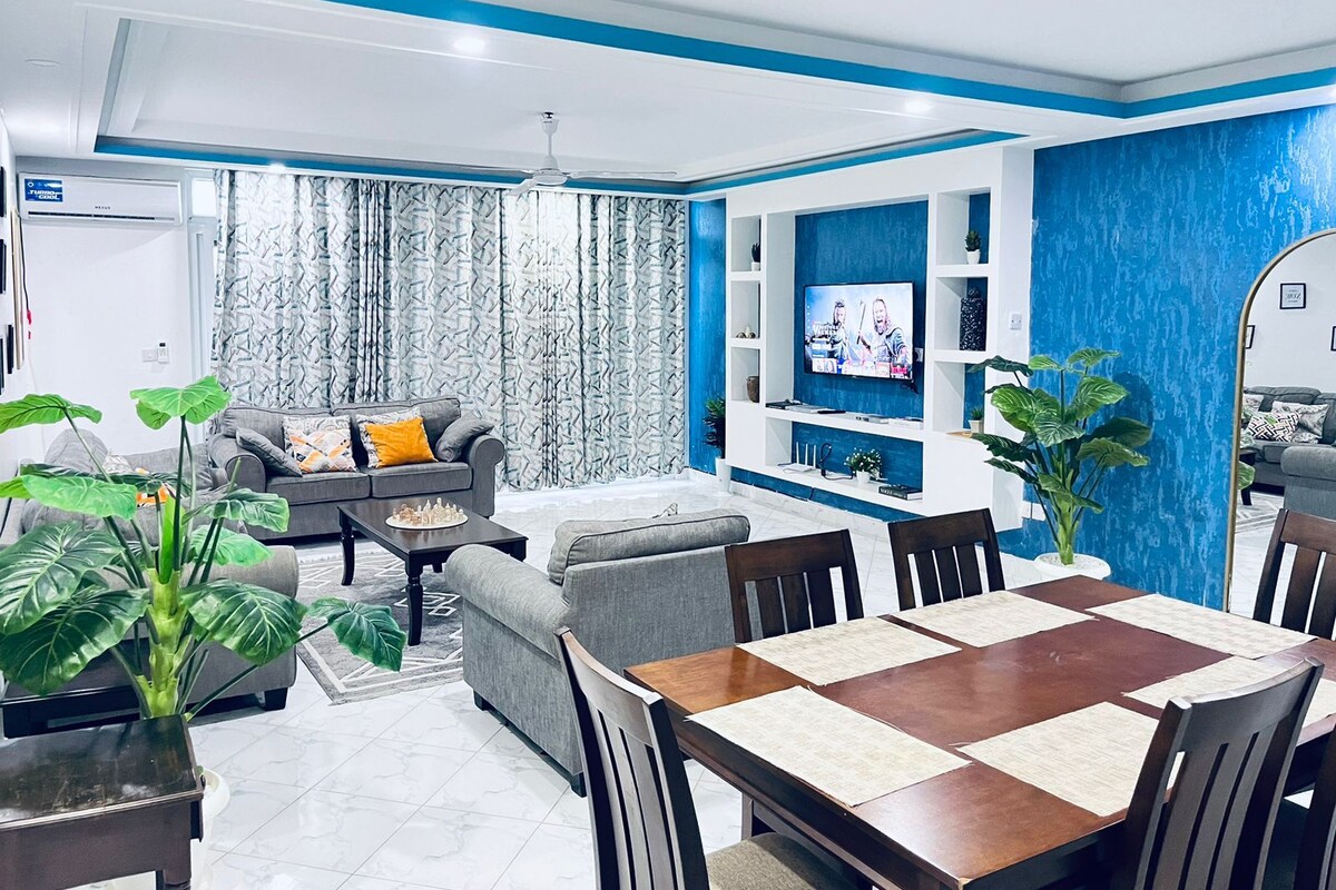 Uma sala de estar moderna com um sofá cinza, uma mesa de centro e uma TV fixada em uma parede azul.