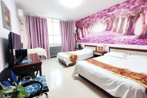Quarto de hotel com duas camas, uma escrivaninha com computador, uma cadeira e um grande mural floral na parede.