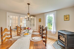 Uma sala de jantar com mesa de madeira posta para quatro pessoas, um candelabro e uma lareira a lenha.