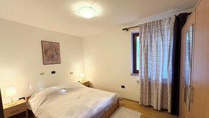 Quarto com cama, abajures, janela com cortinas, luminária no teto e um quadro na parede.