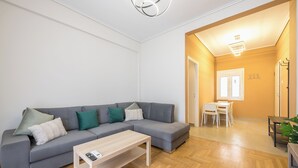 Uma sala de estar moderna com um sofá modular cinza, uma mesa de centro de madeira e um espaço de jantar com uma mesa e cadeiras brancas.