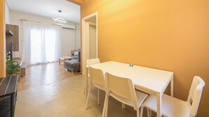 Uma sala de estar moderna com uma mesa de jantar branca e cadeiras, um sofá cinzento e piso de madeira.