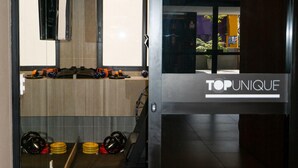 Entrada de hotel com balcão de recepção, uma placa com a inscrição 'TOPUNIQUE' e equipamentos de ginástica visíveis através das portas de vidro.