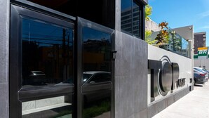 Um edifício moderno com grandes portas de vidro, um carro visível estacionado na frente e uma placa com as letras 'BR' à direita.