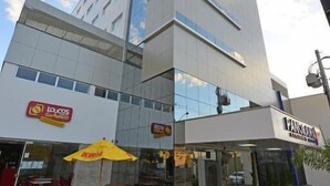 Um edifício moderno com vários andares, área de estar ao ar livre com mesas e cadeiras de madeira e céu claro.