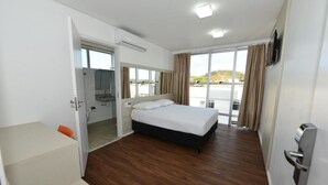 Quarto de hotel com cama, escrivaninha e vista pela janela.