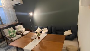 Uma sala de estar moderna com uma mesa de jantar de madeira, um sofá com almofadas decorativas, um vaso de planta e um abajur de chão.