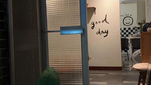 Quarto com uma grande planta em vaso, uma porta de vidro deslizante e uma parede com a placa 'good day'.