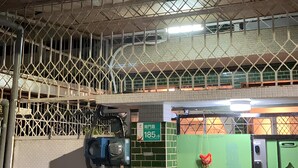 Um edifício com vários andares, entrada com portão, porta verde e placa com o número 185.