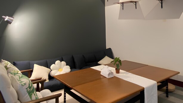 Quarto moderno com parede em tom verde escuro, mesa de madeira, sofá com almofadas e uma pequena planta em vaso.