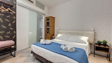 Quarto com cama, guarda-roupa, um banquinho e mesa de cabeceira com plantas.