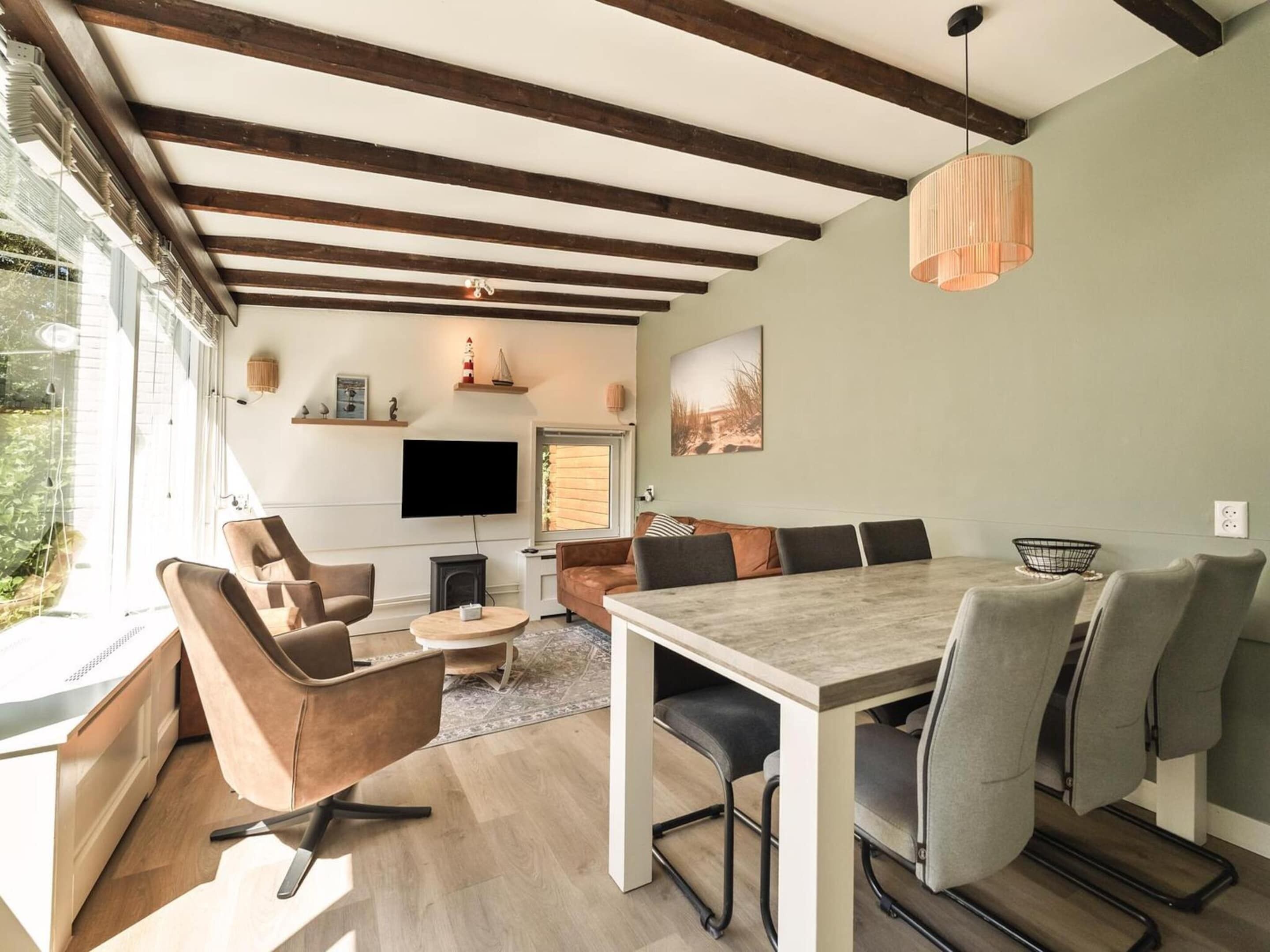 Uma sala de estar moderna com área de jantar, vigas de madeira, uma TV de tela plana e uma janela grande.