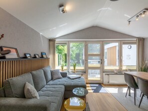 Uma sala de estar moderna com um sofá seccional cinza, uma pequena mesa de centro redonda e uma área de jantar com mesa e cadeiras de madeira.