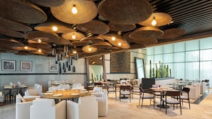 Uma sala de jantar ampla com várias mesas e cadeiras, luminárias de teto feitas de fibra natural e decoração de interiores moderna.