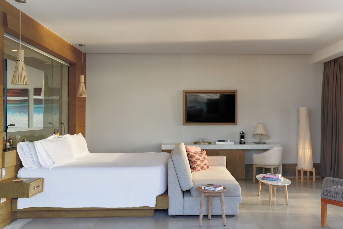 Quarto de hotel moderno com uma cama grande, um sofá, uma escrivaninha e uma televisão.