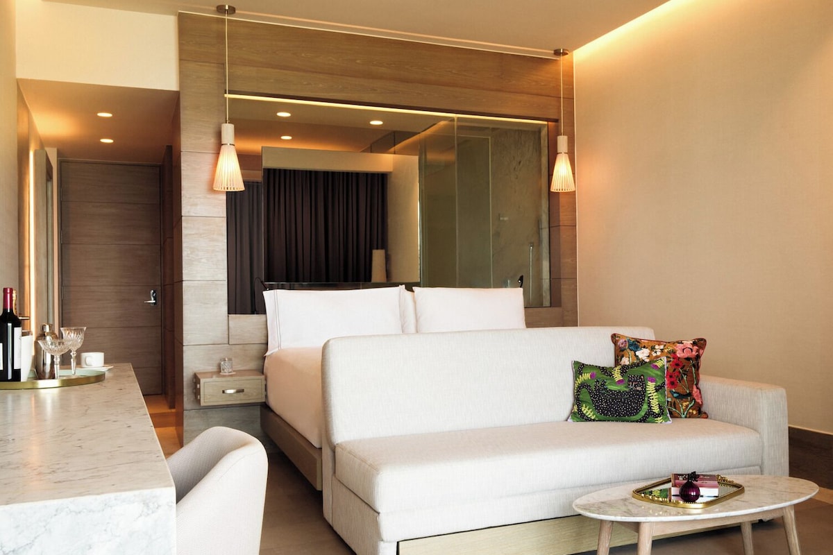 Quarto de hotel moderno com uma cama grande, um sofá, uma mesinha e uma bancada de mármore.