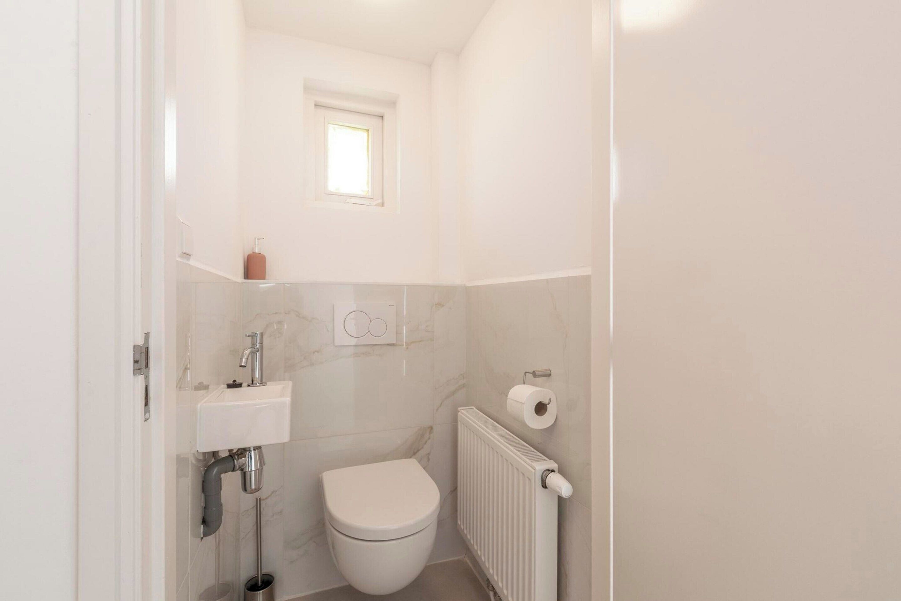 Casa de banho pequena e branca com sanita, lavatório e radiador.