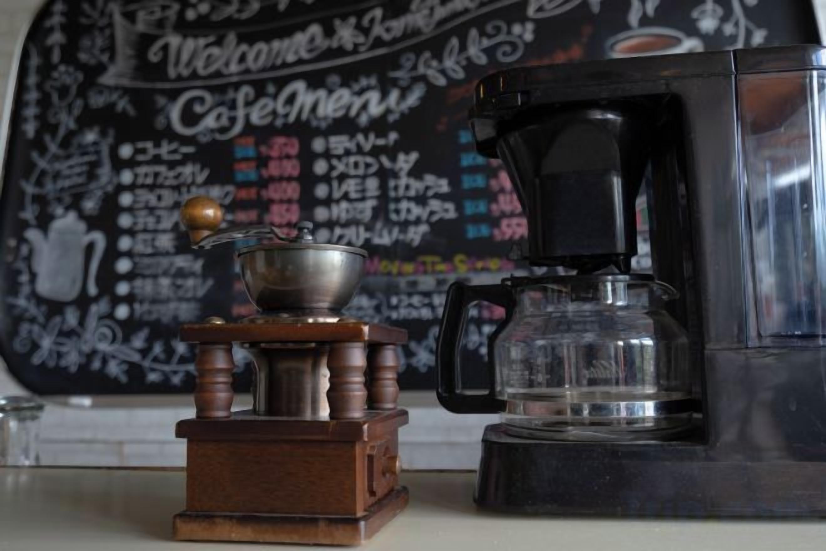 Máquina de café e moedor em balcão, com cardápio em lousa ao fundo.
