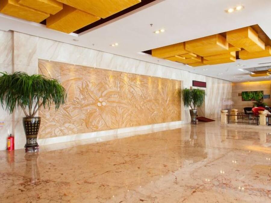 Um hall de hotel com piso de mármore, balcão de recepção e plantas em vasos.