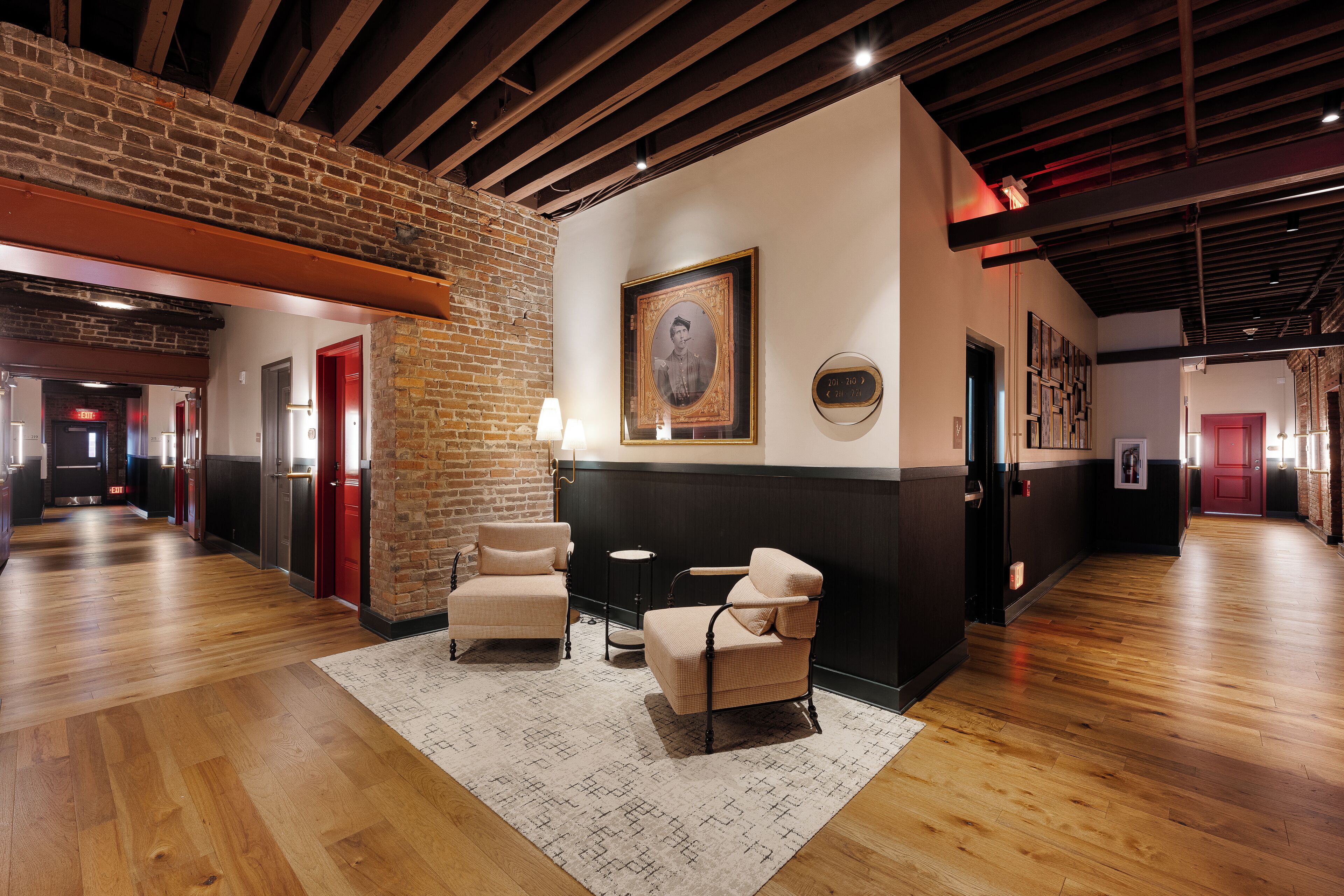Um hall amplo com piso de madeira, parede de tijolos e dois poltronas.