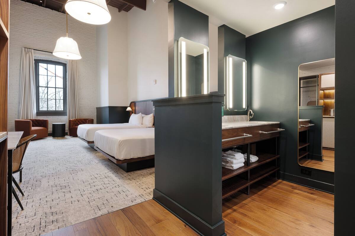 Quarto de hotel moderno com cama, mesas de cabeceira, escrivaninha e um espelho grande.