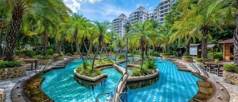 Piscina cercada por palmeiras e um edifício de hotel ao fundo.