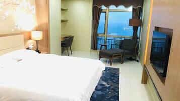 Quarto de hotel com uma cama grande, uma escrivaninha, uma cadeira, televisão e varanda com vista.