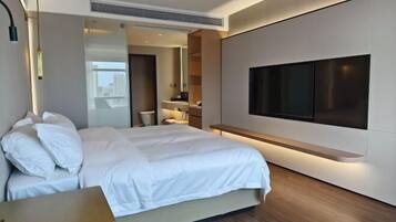 Quarto de hotel moderno com uma cama grande, televisão de tela plana na parede e vista para a cidade pela janela.