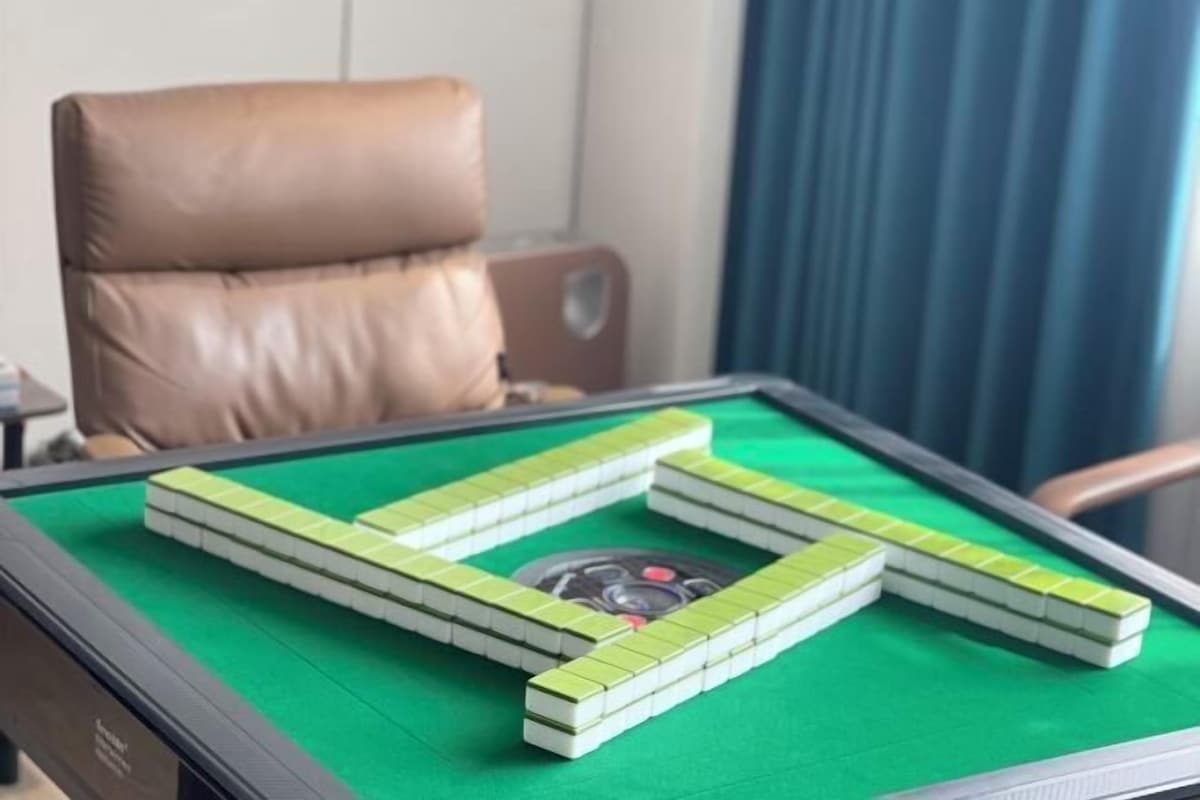Uma mesa de bilhar verde com padrão quadriculado branco e verde, uma poltrona de couro marrom e uma cortina azul ao fundo.