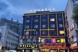 Um hotel com vários andares, letreiros iluminados, diversas janelas e vários estabelecimentos comerciais na base.
