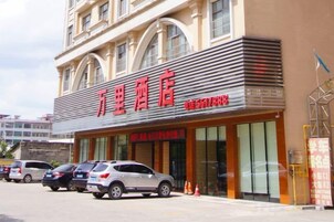 Hotel com placa vermelha chamativa, estacionamento com vários carros e fachada com grandes janelas.