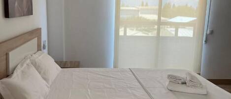 Uma cama bem arrumada com lençóis brancos, cabeceira de madeira e um controle remoto sobre uma mesinha de madeira.