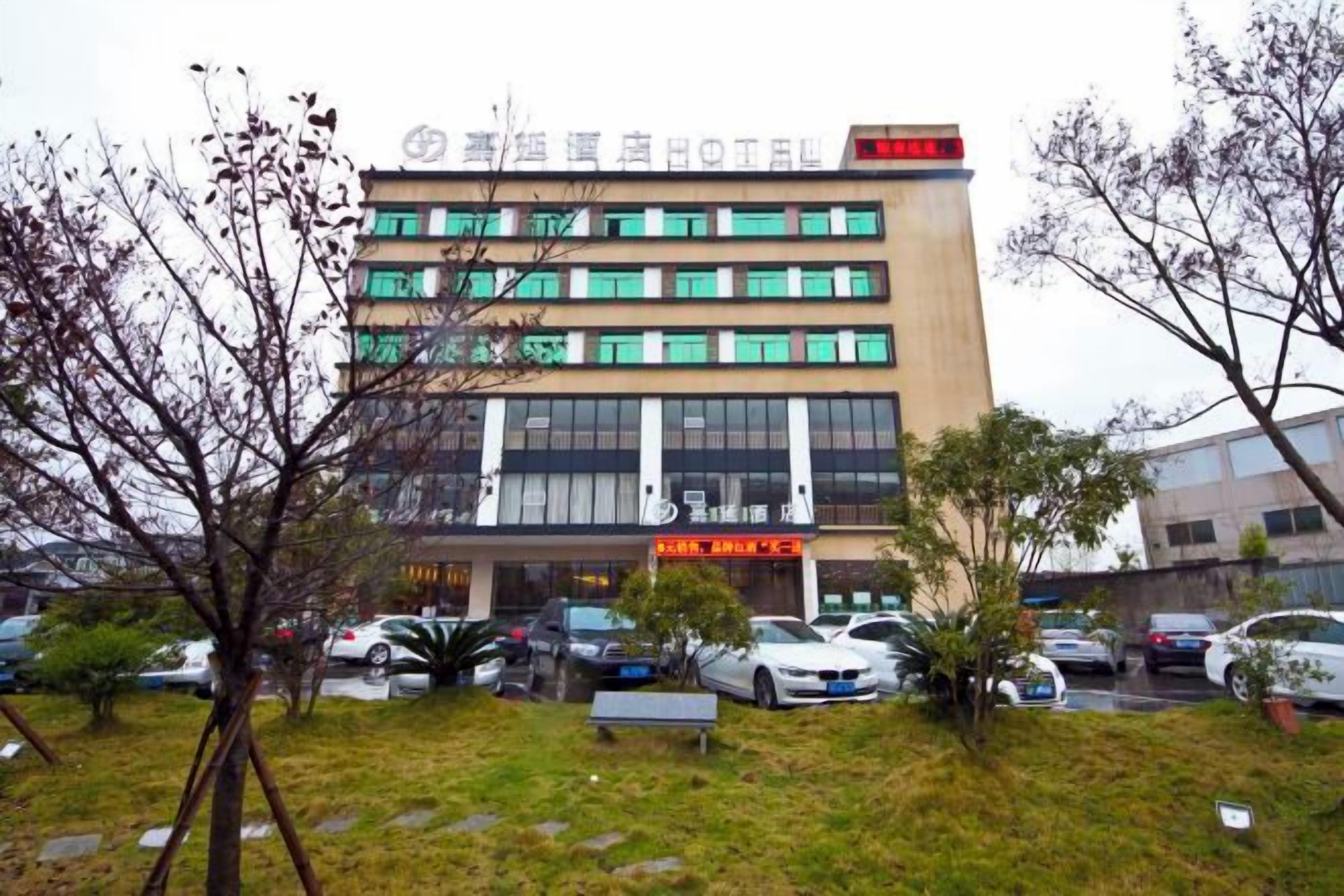 Edifício de hotel com vários andares, estacionamento e algumas árvores em primeiro plano.