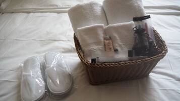 Cama com roupa branca, cesta de vime com produtos de higiene pessoal e um par de chinelos.