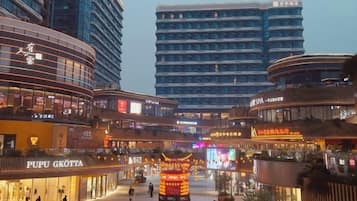 Uma área urbana moderna com arranha-céus, uma praça central com um arco decorativo e diversos estabelecimentos comerciais.