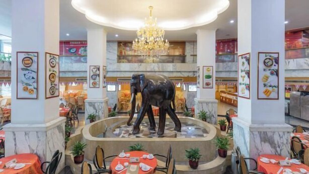 Restaurante com escultura central de elefante, colunas de mármore e um candelabro.