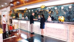 Uma área de recepção de hotel com balcões de mármore, um balcão de atendimento e um funcionário na entrada.