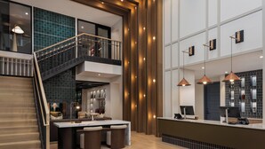 Um saguão de hotel moderno com uma escadaria, uma mesa de recepção e uma área de estar.