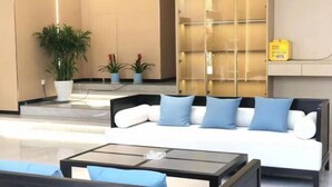 Um lobby moderno com um sofá branco, almofadas azuis, uma mesa de centro e plantas em vasos.