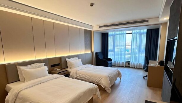 Quarto de hotel com duas camas, uma escrivaninha, uma cadeira, televisão e uma janela grande com cortinas.