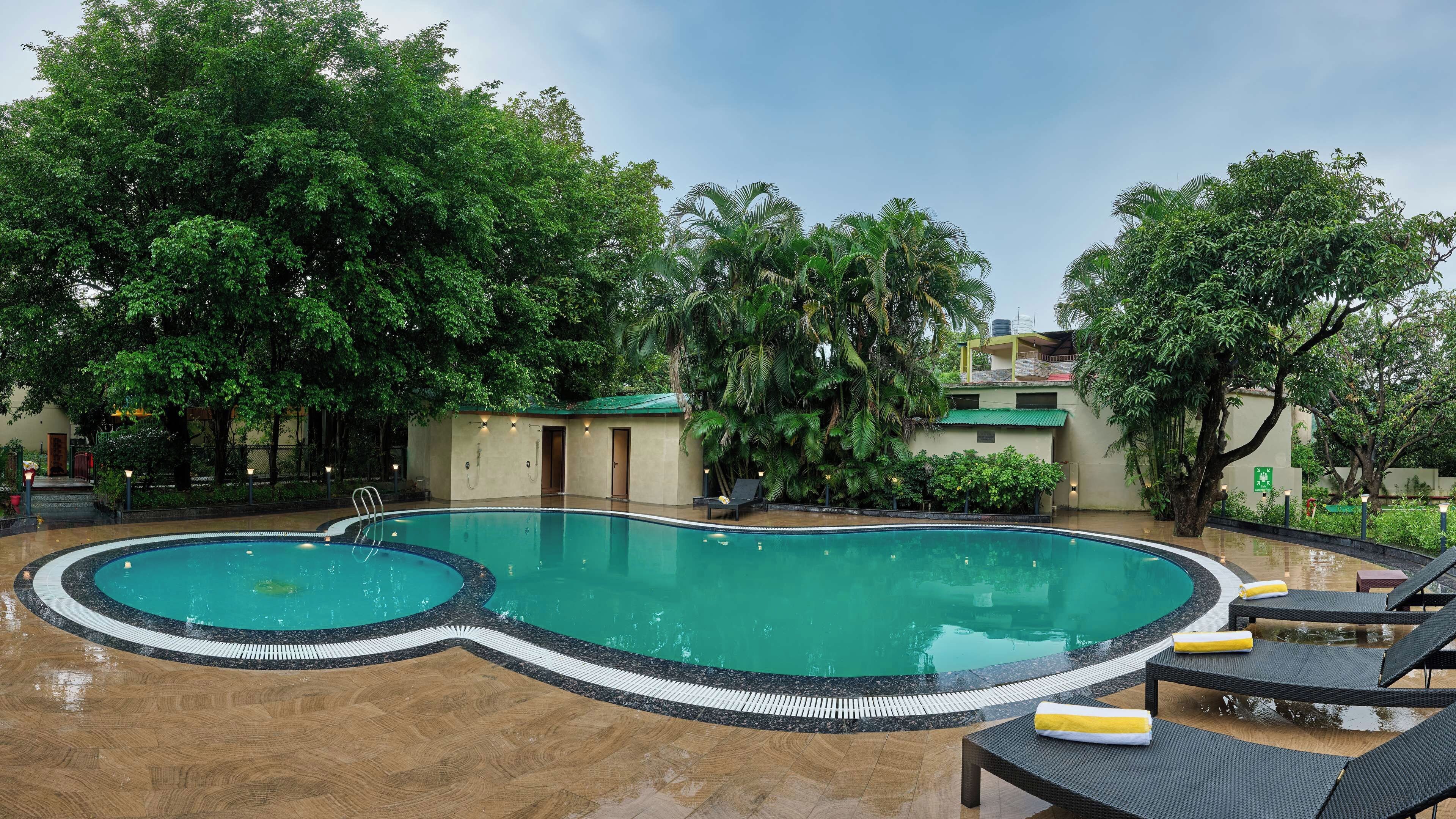 Uma piscina com um deck ao redor, cadeiras de sol e um pequeno edifício com porta e janelas.