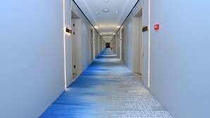 Corredor longo e estreito de um hotel, com carpete azul e paredes brancas.