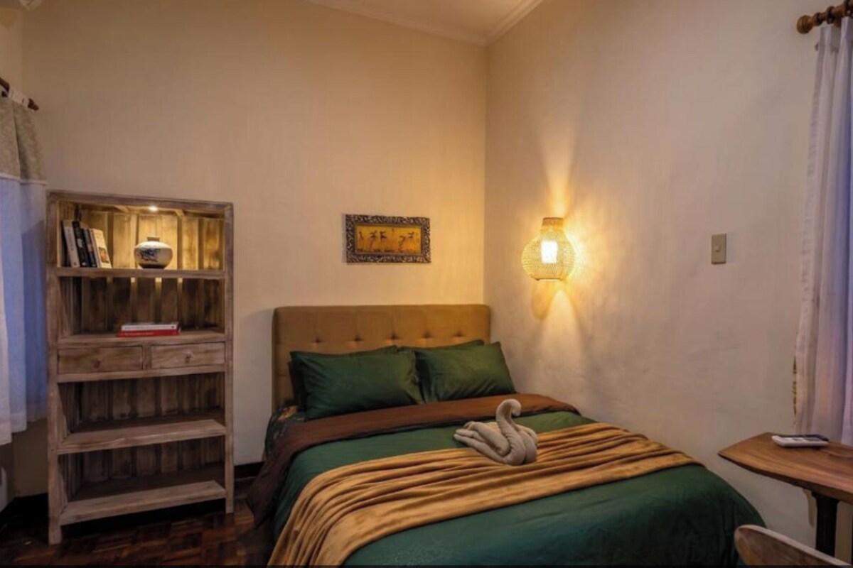 Quarto com cama, estante de madeira, luminária na parede e quadro emoldurado.