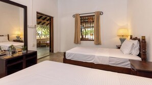 Quarto de hotel com duas camas, ventilador de teto, janela com cortinas, luminária e vista para o exterior.