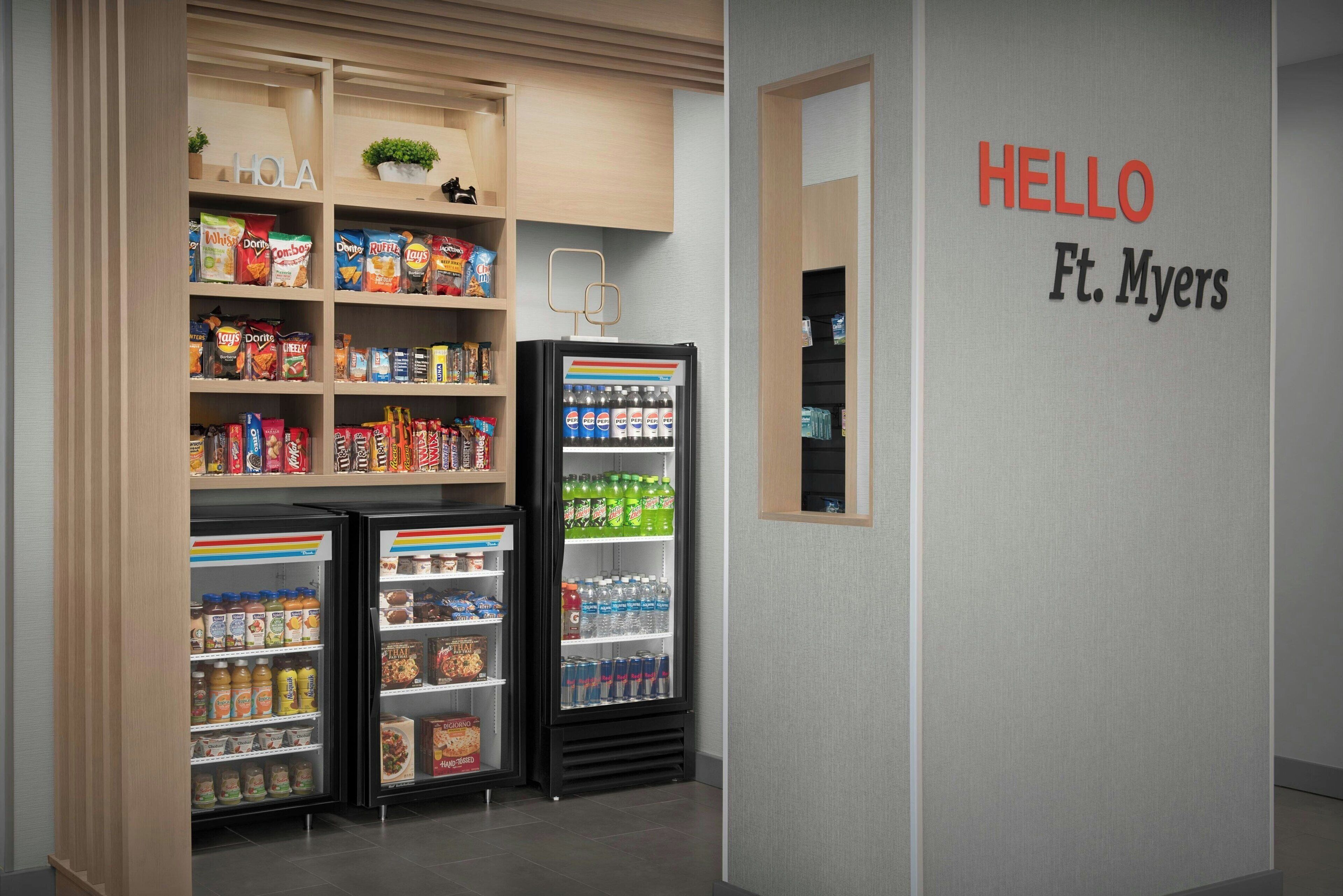 Uma área de distribuição automática com prateleiras cheias de lanches e bebidas, e um letreiro na parede que diz "HELLO Ft. Myers".