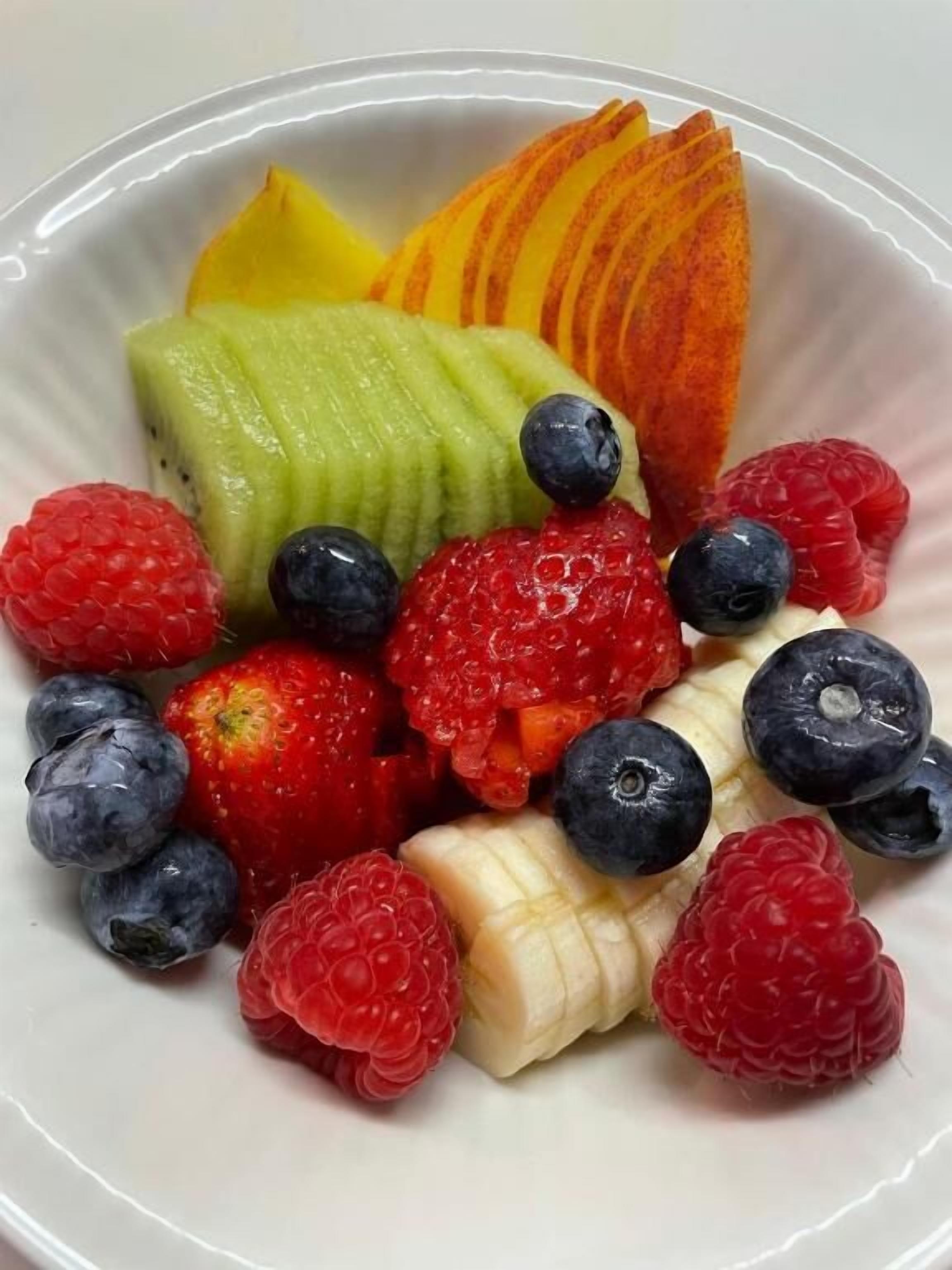 Uma tigela com frutas variadas, incluindo kiwi, morangos, mirtilos, framboesas e fatias de banana.