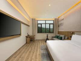 Quarto de hotel moderno com uma cama grande, uma mesa com cadeira, uma mesinha e uma janela ampla com vista para o exterior.