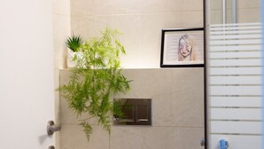 Casa de banho com interruptor de luz na parede, um quadro emoldurado e uma planta em vaso.