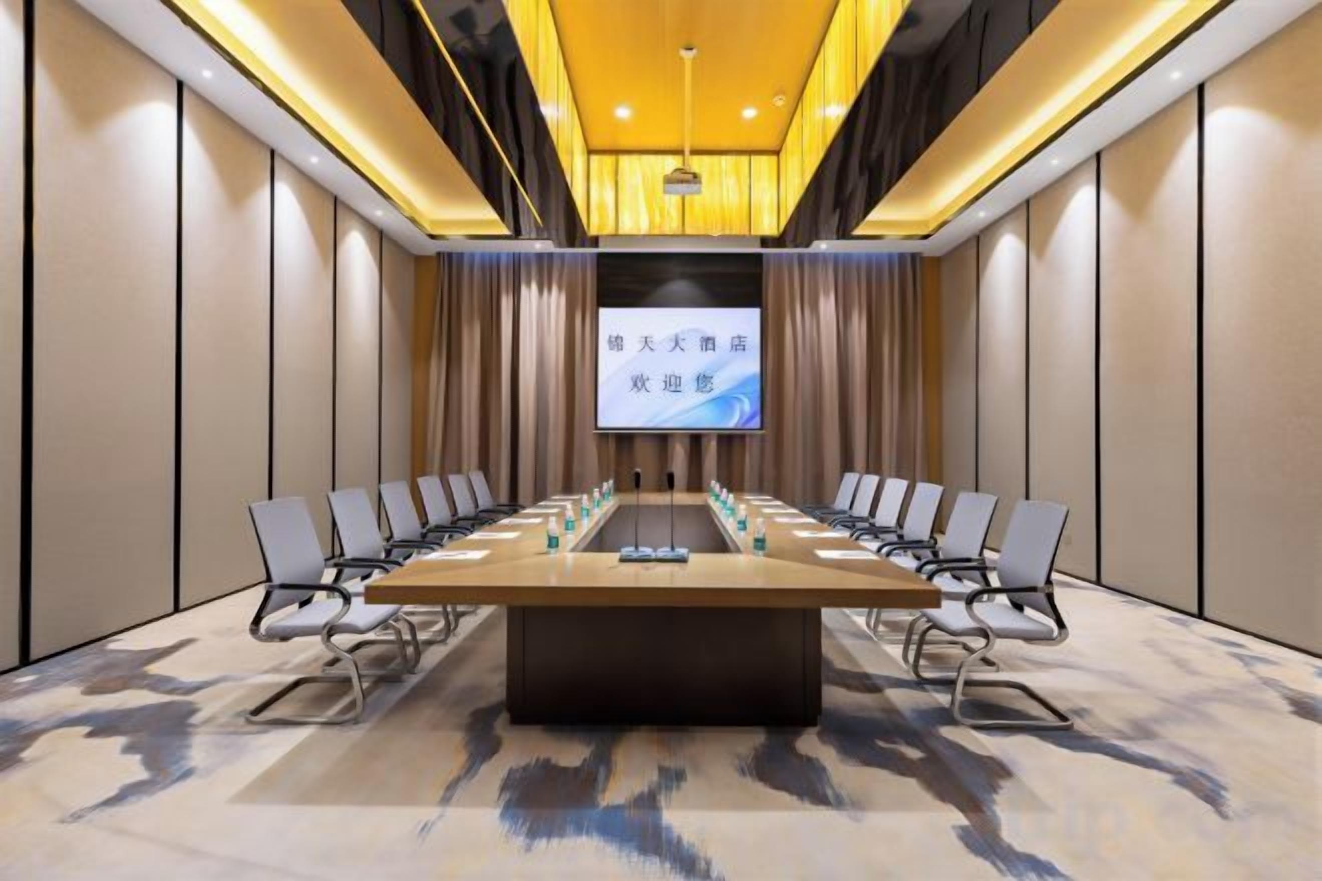 Sala de conferência com uma mesa comprida, cadeiras, tela de projetor e piso coberto de carpete.